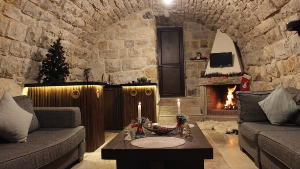 Uma sala de estar acolhedora com paredes de pedra, lareira, dois sofás, uma mesa de centro e um pinheiro de Natal.