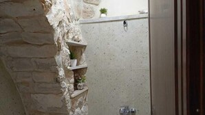 Uma casa de banho com parede de pedra, sanita, chuveiro e porta de madeira.