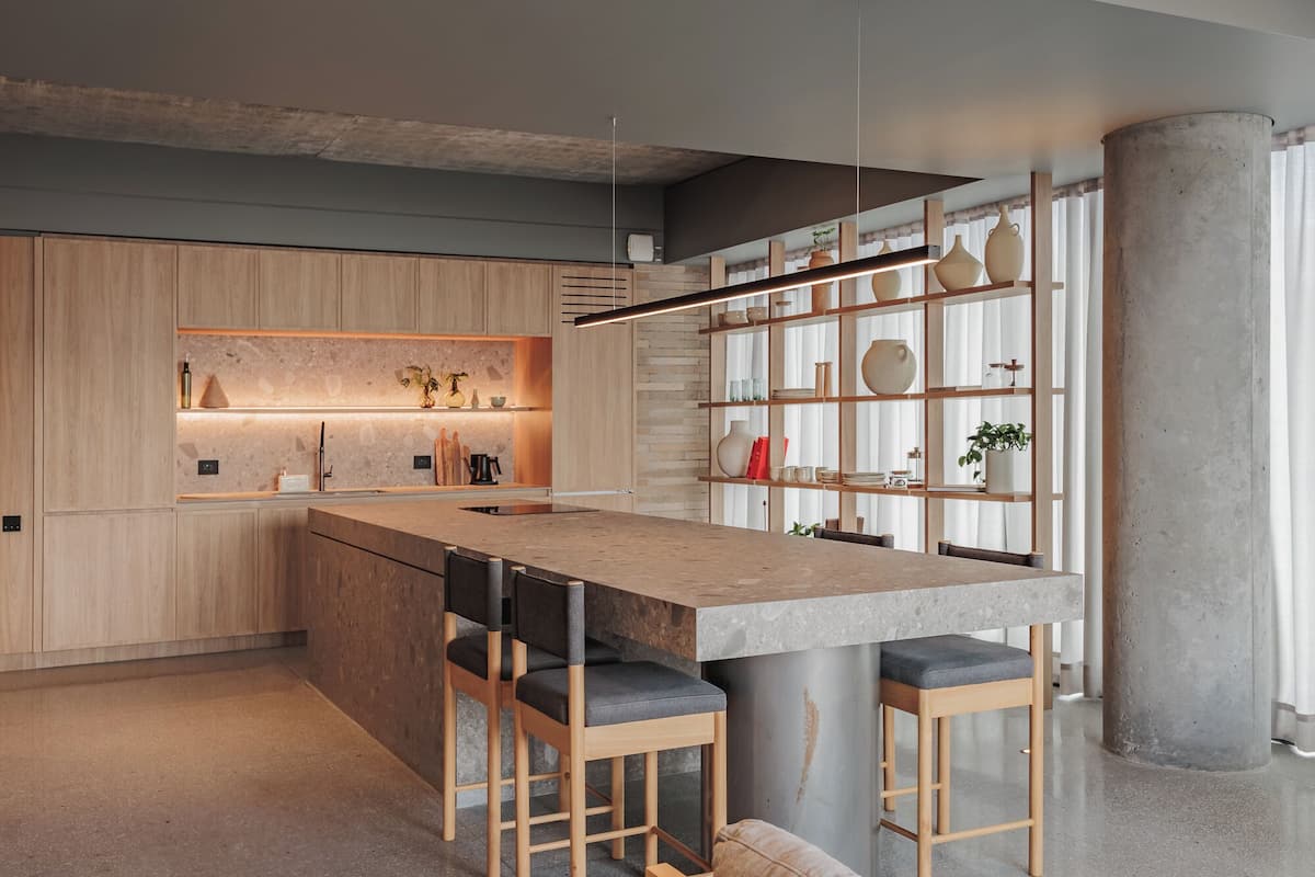 Uma cozinha moderna com uma ilha central, banquetas de bar e uma prateleira embutida com objetos decorativos.
