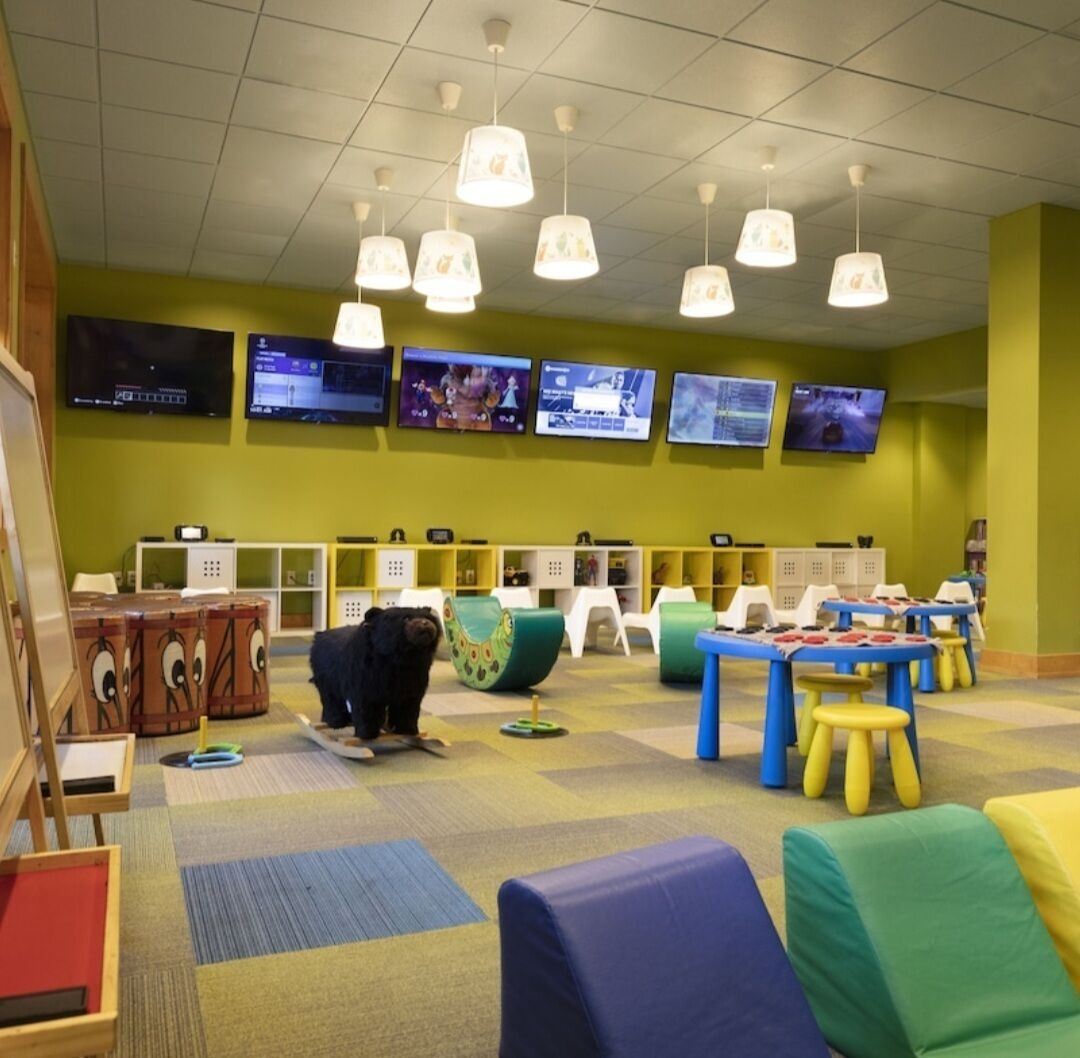 Espaço infantil com mobiliário colorido e várias televisões na parede.