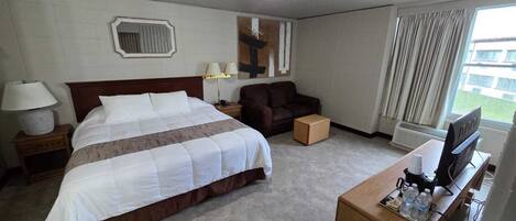 Quarto de hotel com uma cama grande, um sofá, uma escrivaninha com televisão e uma janela com cortinas.