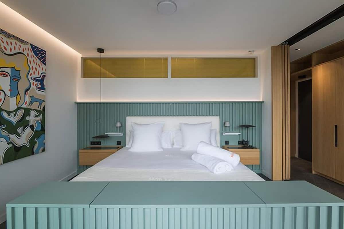 Quarto de hotel moderno com uma cama grande, mesa de cabeceira, televisão presa à parede e um quadro na parede.