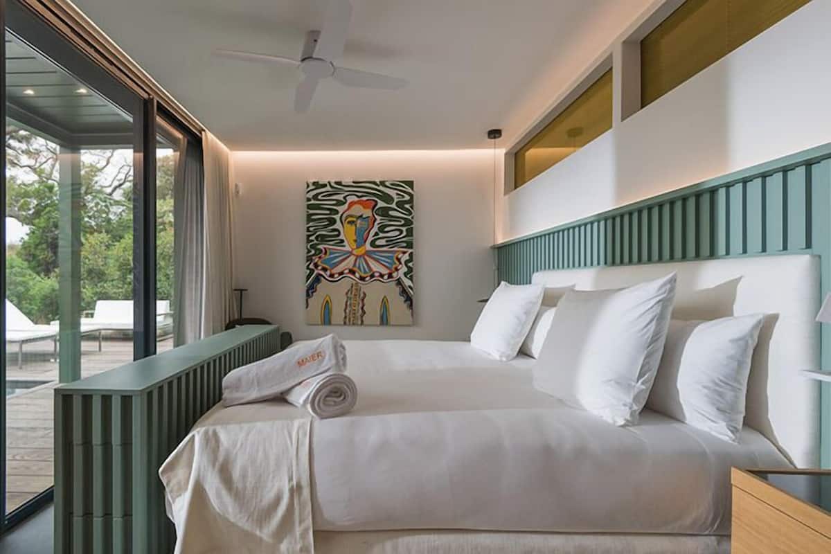 Quarto moderno com uma cama grande, um ventilador de teto, um quadro na parede e vista para o exterior.