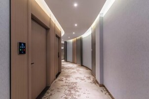 Corredor de hotel com portas, piso coberto por carpete e teto com iluminação embutida.