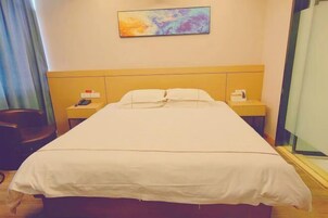 Quarto de hotel com uma cama grande, mesa de cabeceira com telefone, uma cadeira e um quadro na parede.
