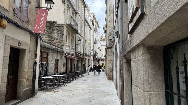 Uma rua estreita com mesas ao ar livre, edifícios de pedra e uma placa vermelha.