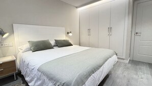 Quarto com cama, mesas de cabeceira, luminárias de parede e guarda-roupa.