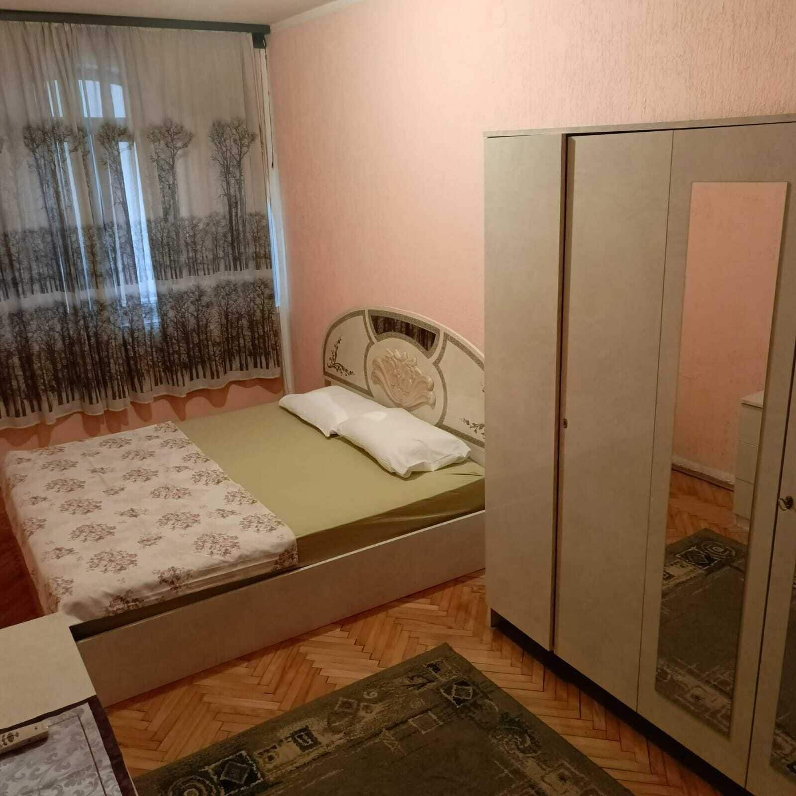 Quarto com cama, guarda-roupa, janela com cortina e tapete estampado.