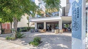 Entrada de hotel com área de estar ao ar livre, varanda coberta e um grande letreiro.