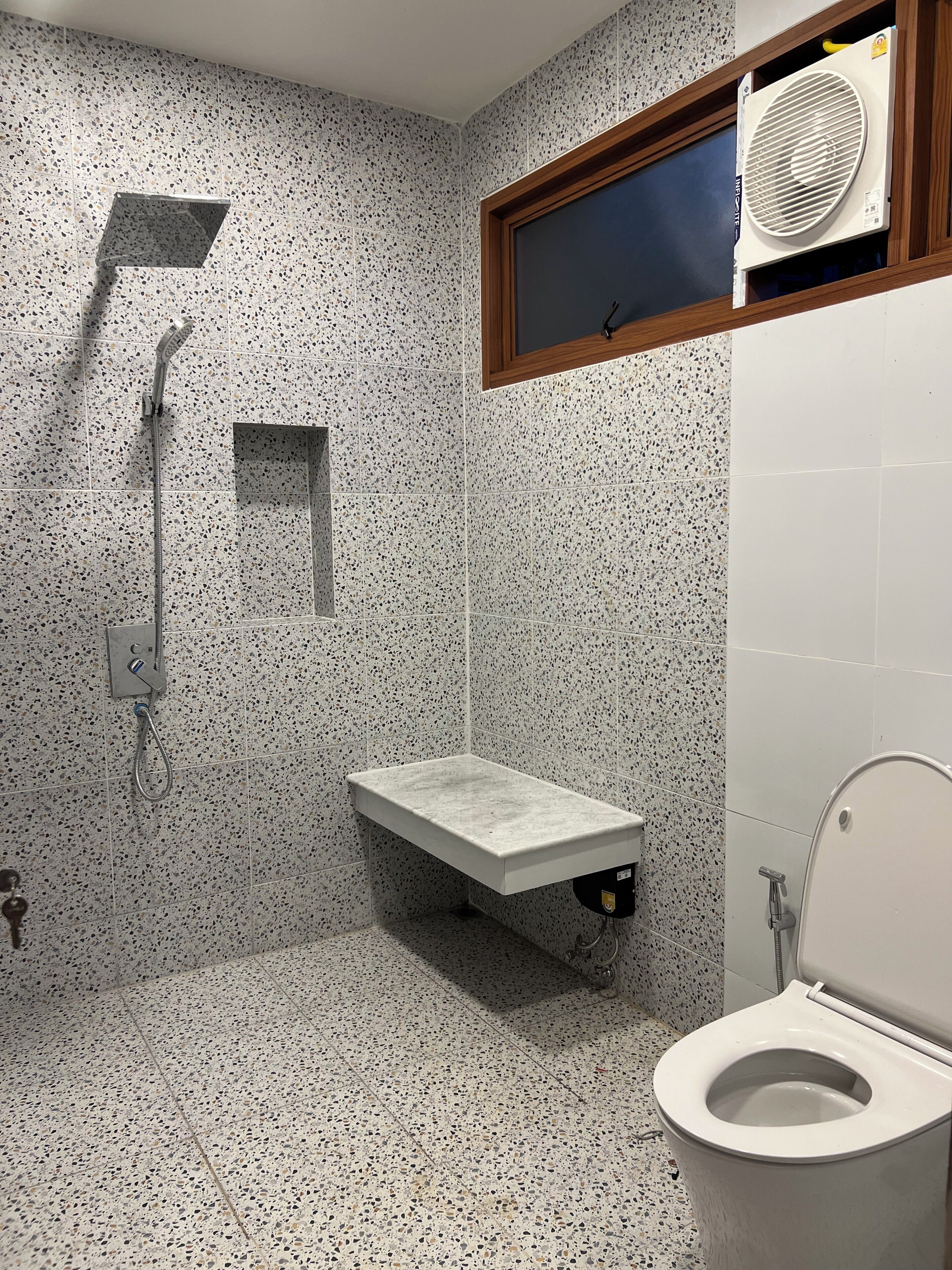 Casa de banho com sanita independente, chuveiro com flexa, lavatório embutido e ar condicionado fixado na parede.