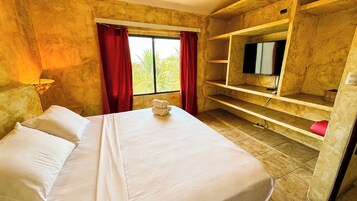 Quarto de hotel com cama, televisão em uma estante e janela com cortinas.