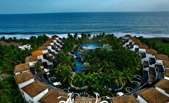 Resort com piscina central cercada por palmeiras e vista para o mar.