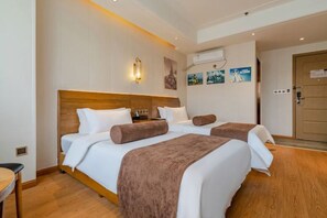Quarto de hotel com duas camas, cabeceiras de madeira, roupa de cama branca, manta marrom, ar condicionado fixado na parede e porta com puxador.