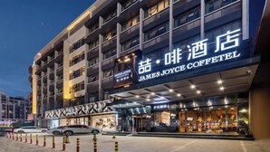 Um hotel com vários andares, uma placa chamativa para James Joyce Caffeetel e um estacionamento com carros.