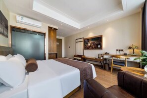 Quarto de hotel com cama, escrivaninha, cadeira e sofá.