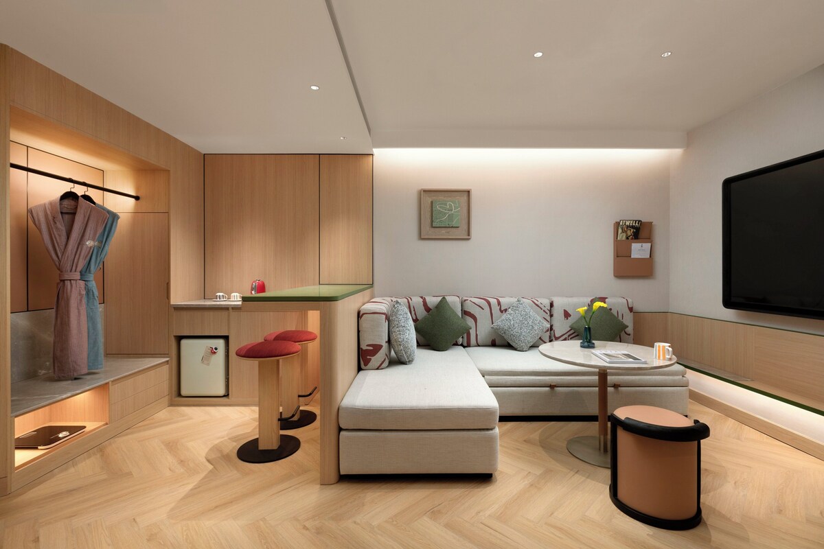 Uma sala de estar moderna com um sofá, uma mesa pequena, uma televisão e um espaço com cozinha compacta.