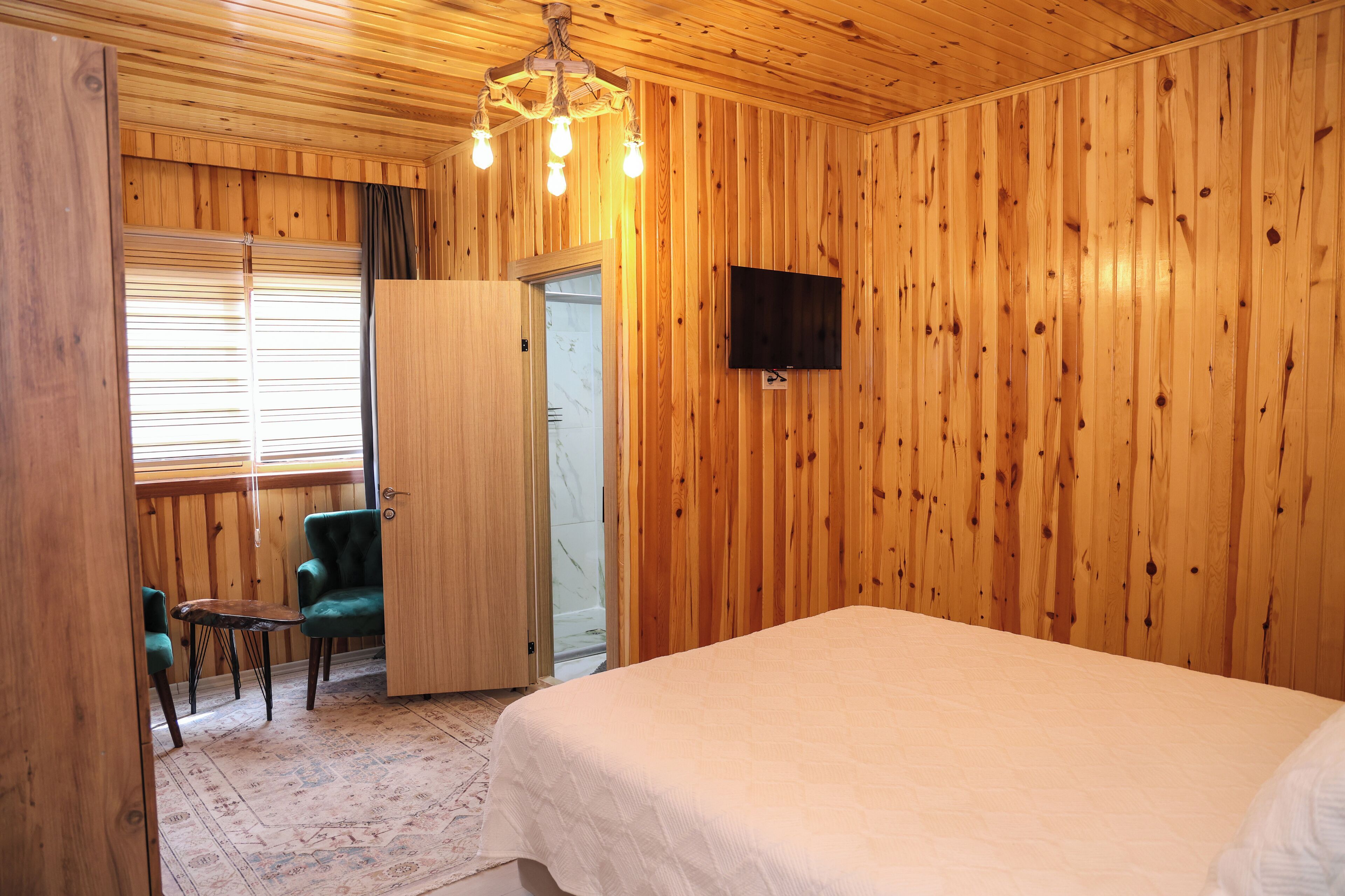 Quarto com painéis de madeira, uma cama, televisão na parede e uma pequena mesa com duas cadeiras.