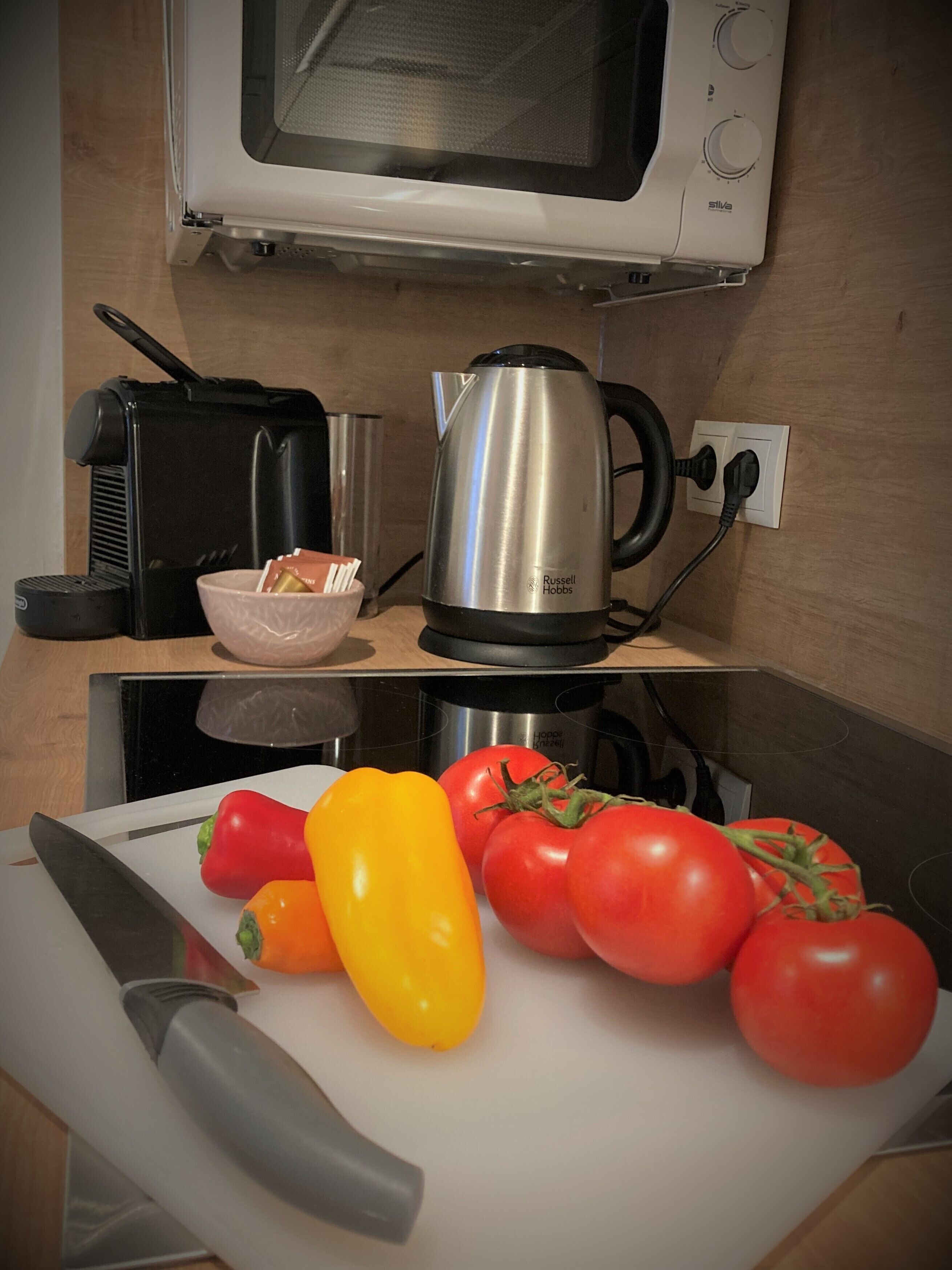 Cozinha equipada com micro-ondas, cafeteira, chaleira e legumes frescos na bancada.