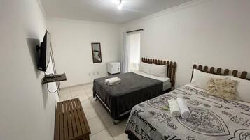 Quarto de hotel com duas camas, televisão de tela plana, uma mesa pequena e janela com cortinas.