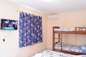 Quarto com cama beliche, televisão na parede e cortina florida.