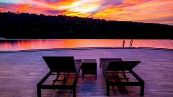 Vista do pôr do sol com três cadeiras de lounge e uma pequena mesa em um deck revestido com azulejos.