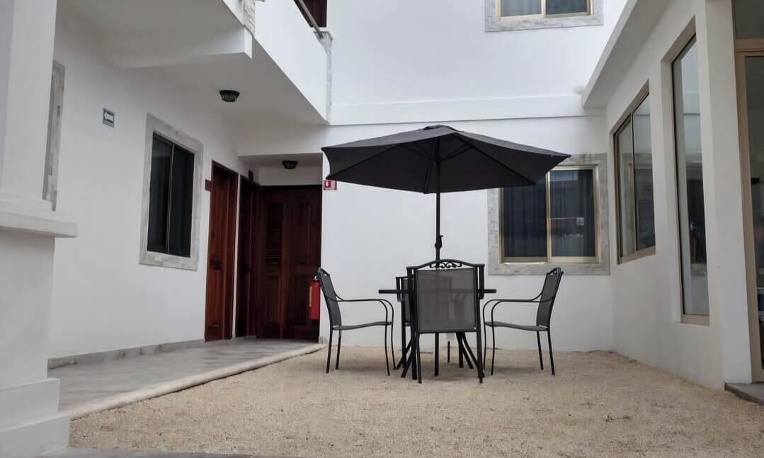 Uma área de varanda coberta com mesa e cadeiras, um guarda-sol preto e uma porta que dá para o interior.