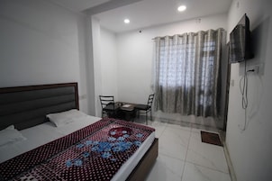 Quarto com cama, escrivaninha e televisão.