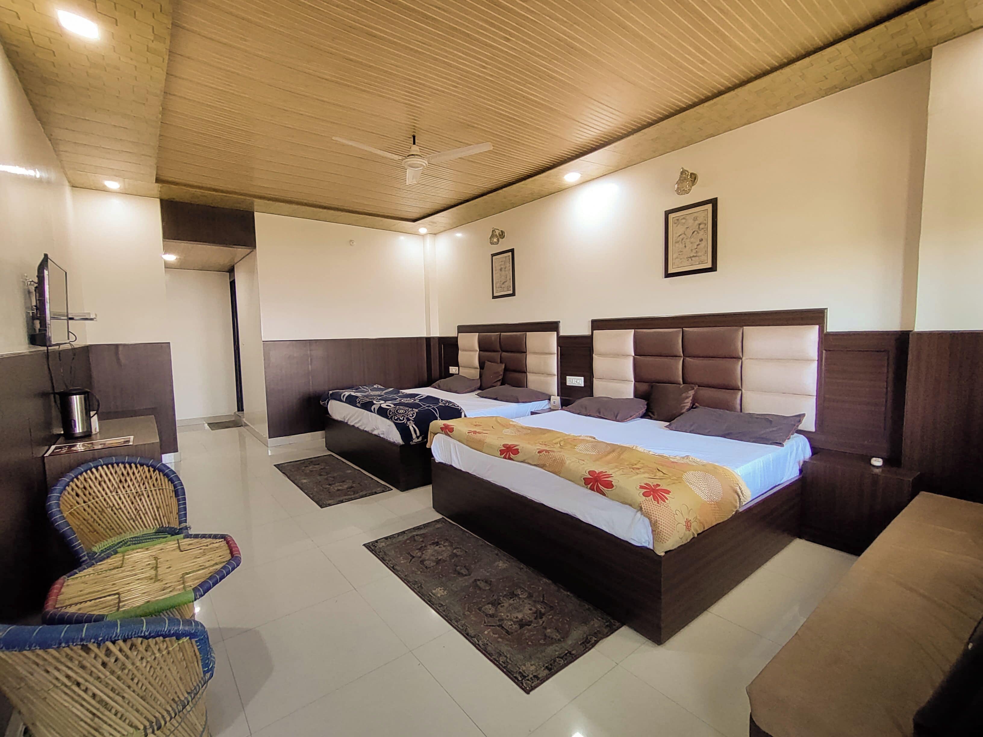 Quarto de hotel com duas camas, uma escrivaninha, uma cadeira e um ventilador de teto.