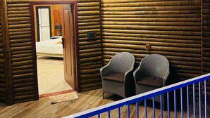 Quarto em estilo cabana de tronco com porta de madeira, uma cama e duas cadeiras de vime.