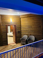 Quarto em estilo cabana de tronco com porta de madeira, uma cama e duas cadeiras de vime.