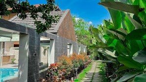Um caminho bordeado por plantas tropicais que leva a um edifício moderno com telhado em azulejos.