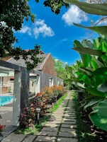 Um caminho bordeado por plantas tropicais que leva a um edifício moderno com telhado em azulejos.