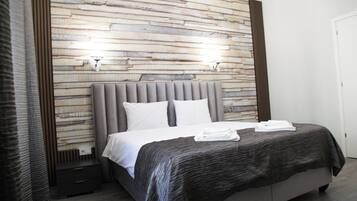 Quarto moderno com painel de parede de madeira, cabeceira estofada cinza, roupa de cama branca e uma pequena mesa de cabeceira.