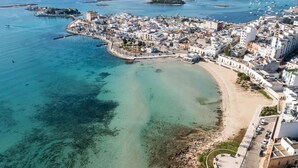Vista aérea de uma cidade costeira com praia, águas cristalinas e uma mistura de edifícios residenciais e comerciais.