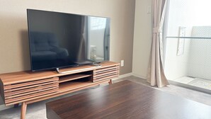 Sala moderna com televisão de tela plana em um móvel de madeira, mesa de centro de madeira escura e vista para uma varanda através de uma janela com cortinas.