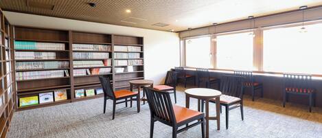 Uma biblioteca com estantes, cadeiras, mesas e janelas amplas.