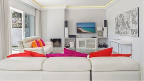Uma sala de estar moderna com um sofá branco, almofadas coloridas, televisão de tela plana e obras de arte nas paredes.