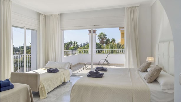 Quarto de hotel com duas camas, uma varanda e vista para palmeiras.