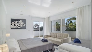 Quarto de hotel moderno com cama, sofá, mesa e varanda com vista.