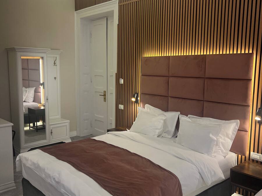 Quarto de hotel com uma cama grande, um guarda-roupa, um espelho e uma mesa de cabeceira com abajur.