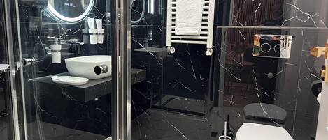 Uma casa de banho moderna com chuveiro em cabine de vidro, uma pia branca, sanita e suporte para toalhas.