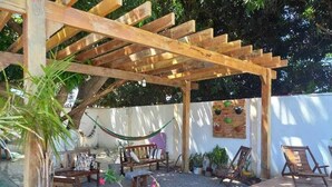 Uma pérgola de madeira com uma rede, área de estar ao ar livre e vasos de plantas.