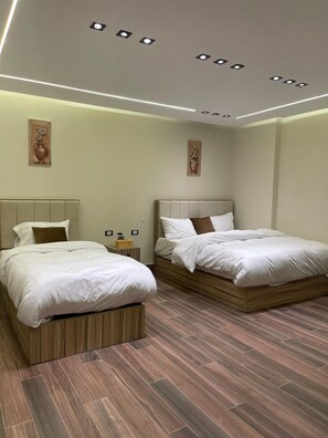 Quarto moderno com duas camas, cabeceiras de madeira e luminária embutida no teto.