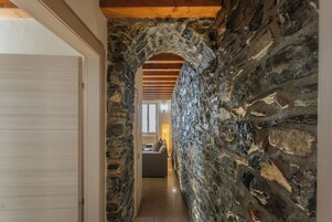 Corredor de paredes de pedra que dá para uma sala de estar com um sofá e uma luminária.