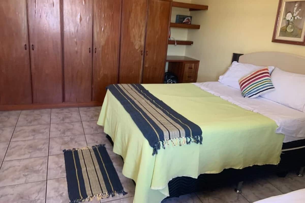 Quarto com uma cama, guarda-roupa de madeira, uma mesinha e prateleira na parede.