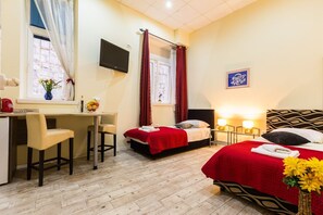Quarto de hotel com uma mesa, duas camas, uma televisão e uma janela com cortinas.