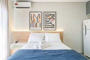 Quarto de hotel com cama, almofadas brancas, cobertor azul e duas obras de arte minimalistas nas paredes.