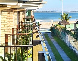 Um hotel à beira-mar com varanda com vista para o mar, um caminho que leva à praia e uma construção com telhado de palha.