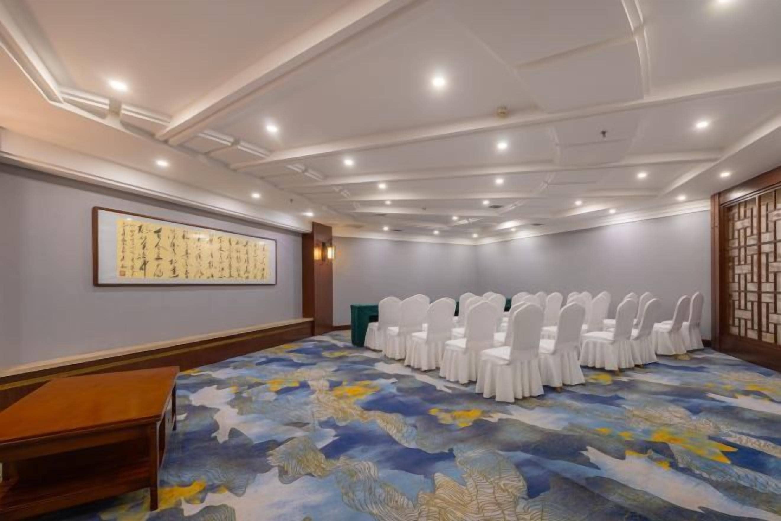 Uma sala de conferências com carpete estampado, cadeiras brancas e uma grande obra de arte emoldurada na parede.