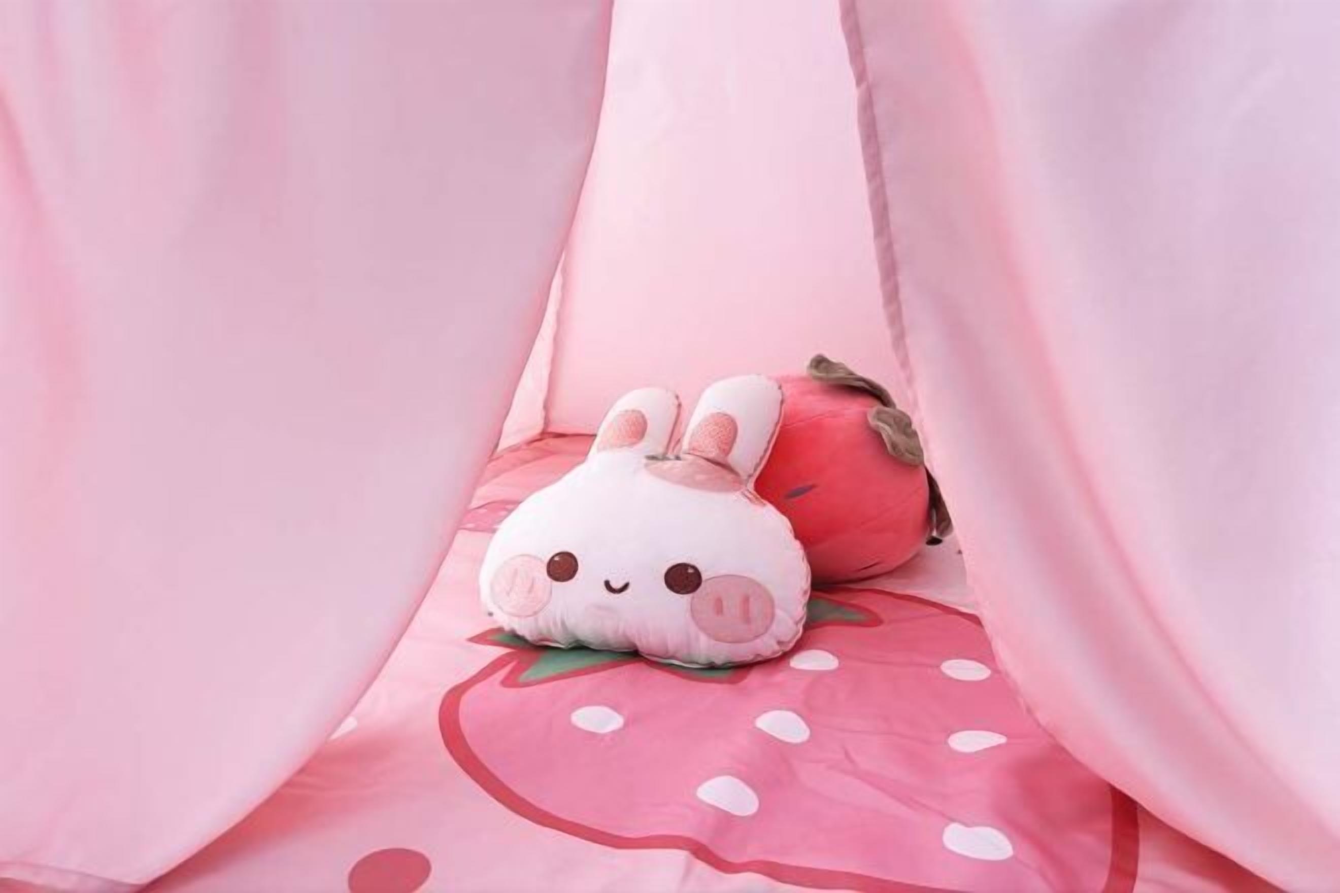 Uma cama rosa com um travesseiro em formato de morango e um brinquedo de pelúcia branco que se assemelha a um coelho.
